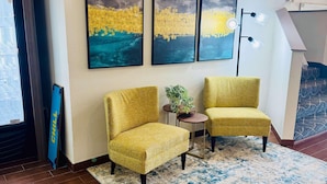 Um quarto com duas poltronas amarelas, uma mesa pequena com uma planta e três obras de arte emolduradas na parede.