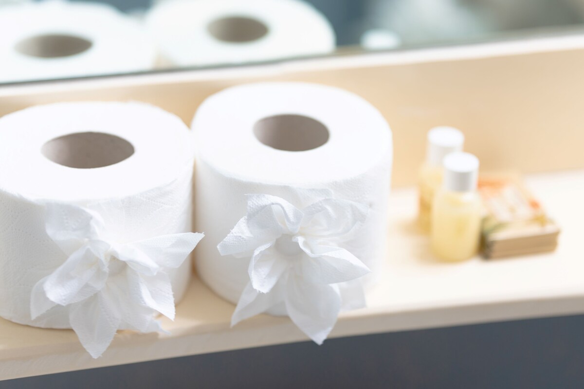 Dois rolos de papel higiênico com fitas, uma garrafa pequena e uma caixa sobre uma superfície de madeira.