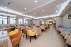 Uma sala de jantar ampla, com várias mesas e cadeiras, janelas grandes e design moderno no teto.