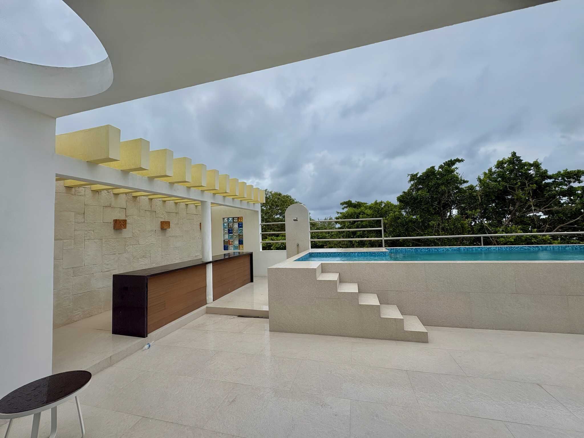 Uma área moderna de piscina ao ar livre, com um muro de pedra, um bar de madeira e uma escadaria que dá para a piscina.