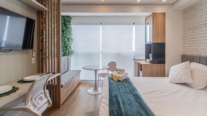 Quarto de hotel moderno com cama, TV, área de estar e varanda com vista.