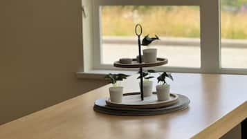 Uma mesa de madeira com um suporte escalonado para pequenos vasos de plantas, colocada perto de uma janela com vista para vegetação e montanhas.