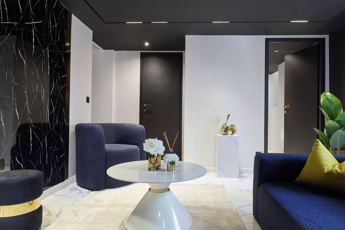 Uma sala de estar moderna com parede de mármore, mesa de centro redonda, sofá azul e porta escura.
