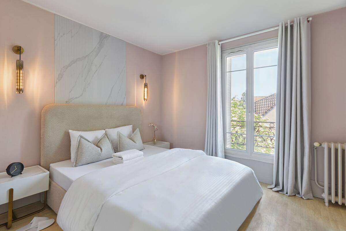 Quarto bem organizado com uma cama grande, luminárias de cabeceira, mesa de cabeceira e uma janela com cortinas.