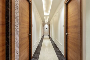 Um corredor comprido e estreito com portas de madeira e chão de mármore.