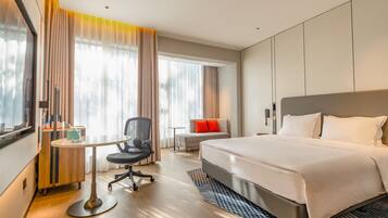 Quarto de hotel com uma cama grande, uma escrivaninha, uma cadeira e um sofá.