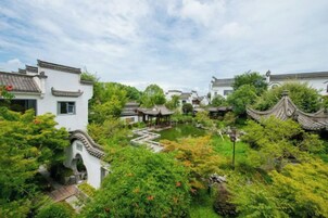 Um pátio tradicional com edifícios, um lago e vegetação exuberante.