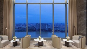Um lounge moderno com vista panorâmica da cidade, apresentando um sofá curvo e um piso com padrão marmorizado.
