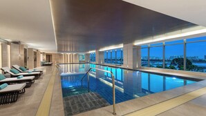 Piscina interior moderna com espreguiçadeiras e vista para a cidade.