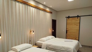 Quarto de hotel com duas camas, cabeceira de madeira, porta deslizante e um banquinho de madeira.