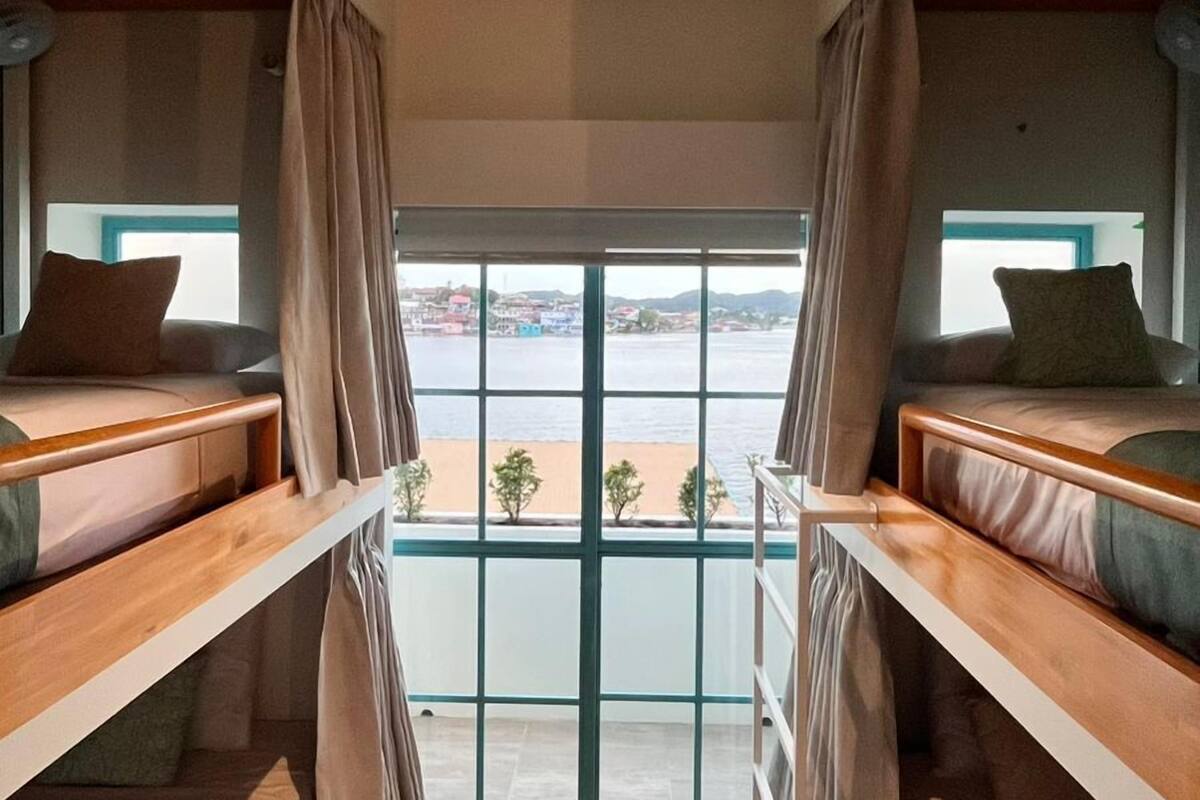 Quarto com duas beliches, janela com vista para um corpo d'água e uma luminária no teto.