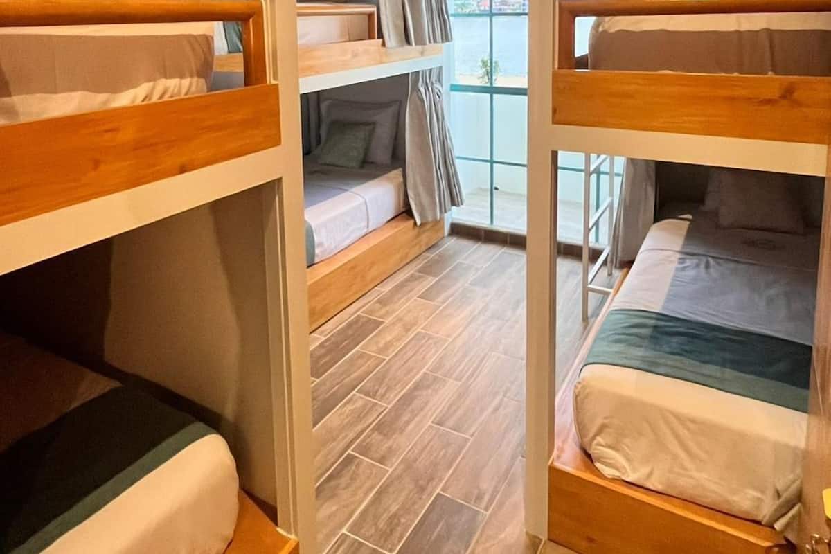 Quarto com beliches, janela com cortinas e piso de azulejos.