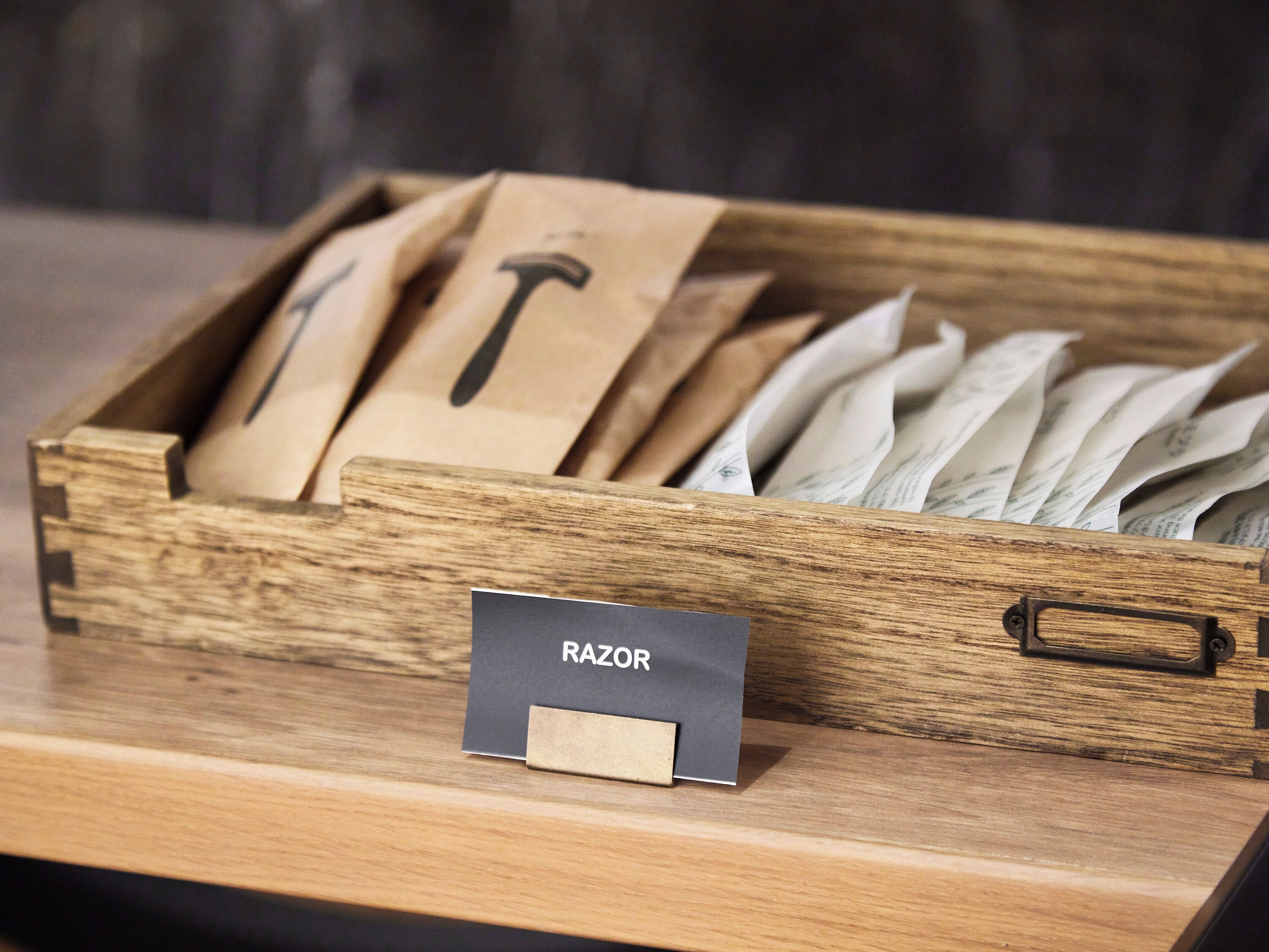 Uma caixa de madeira com divisórias rotuladas como "RAZOR", contendo diversos artigos de higiene pessoal.