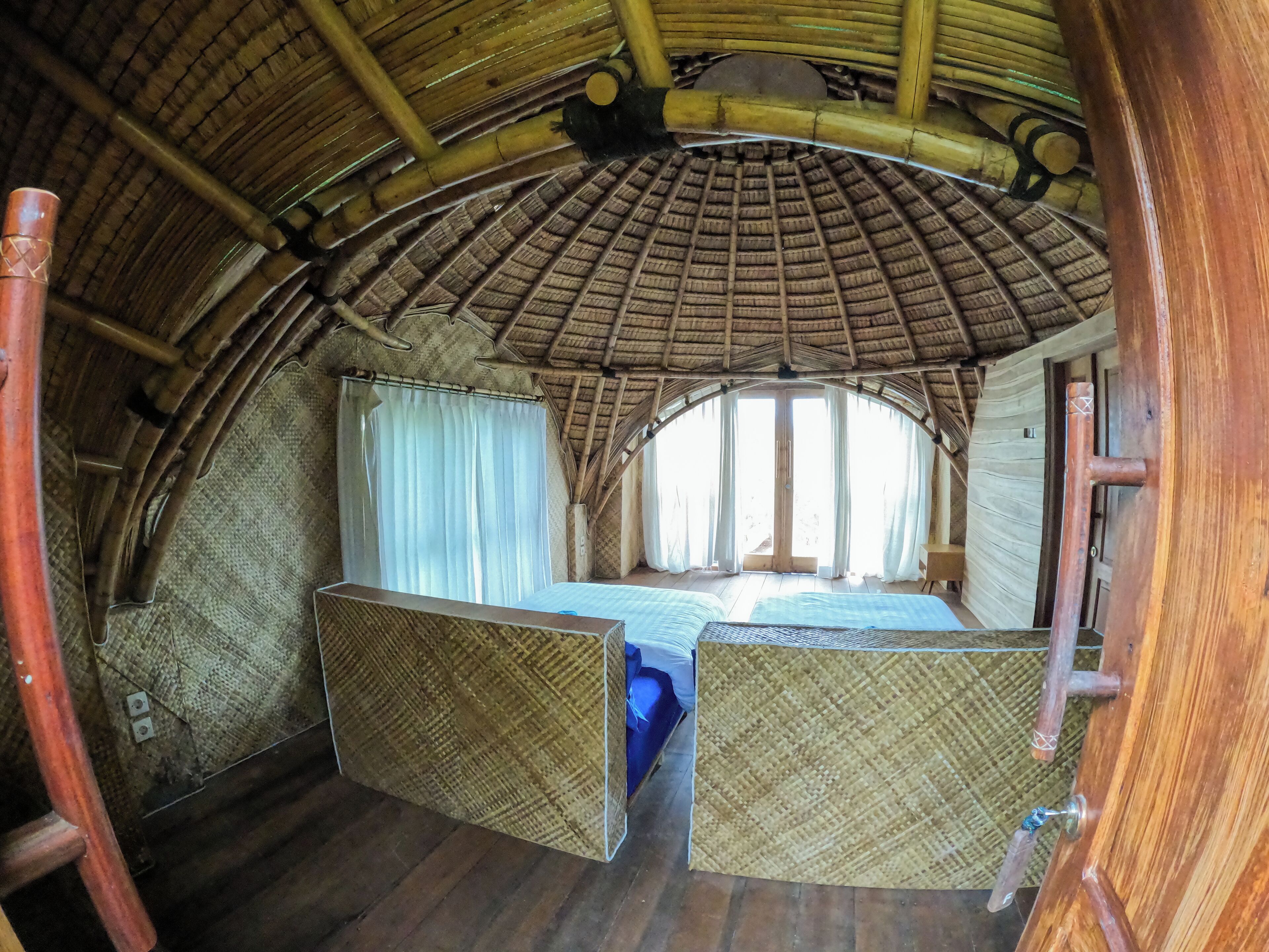 Um quarto acolhedor com telhado de palha, uma cama, uma janela com cortinas e uma porta de madeira.