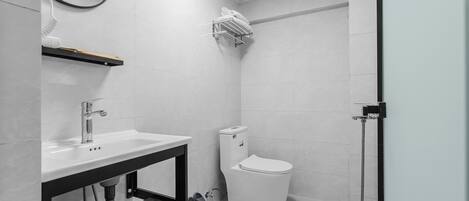 Uma casa de banho moderna com lavatório, sanita e chuveiro brancos.