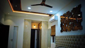 Quarto com cabeceira estofada, ventilador de teto, iluminação embutida e espelho fixado na parede.