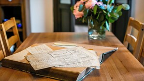 Uma mesa de madeira com um jornal, um livro e um vaso de flores.