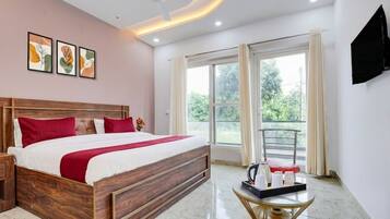 Quarto de hotel com cama de madeira, uma mesa redonda pequena com um tabuleiro, ventoinha no teto e uma janela grande com cortinas.
