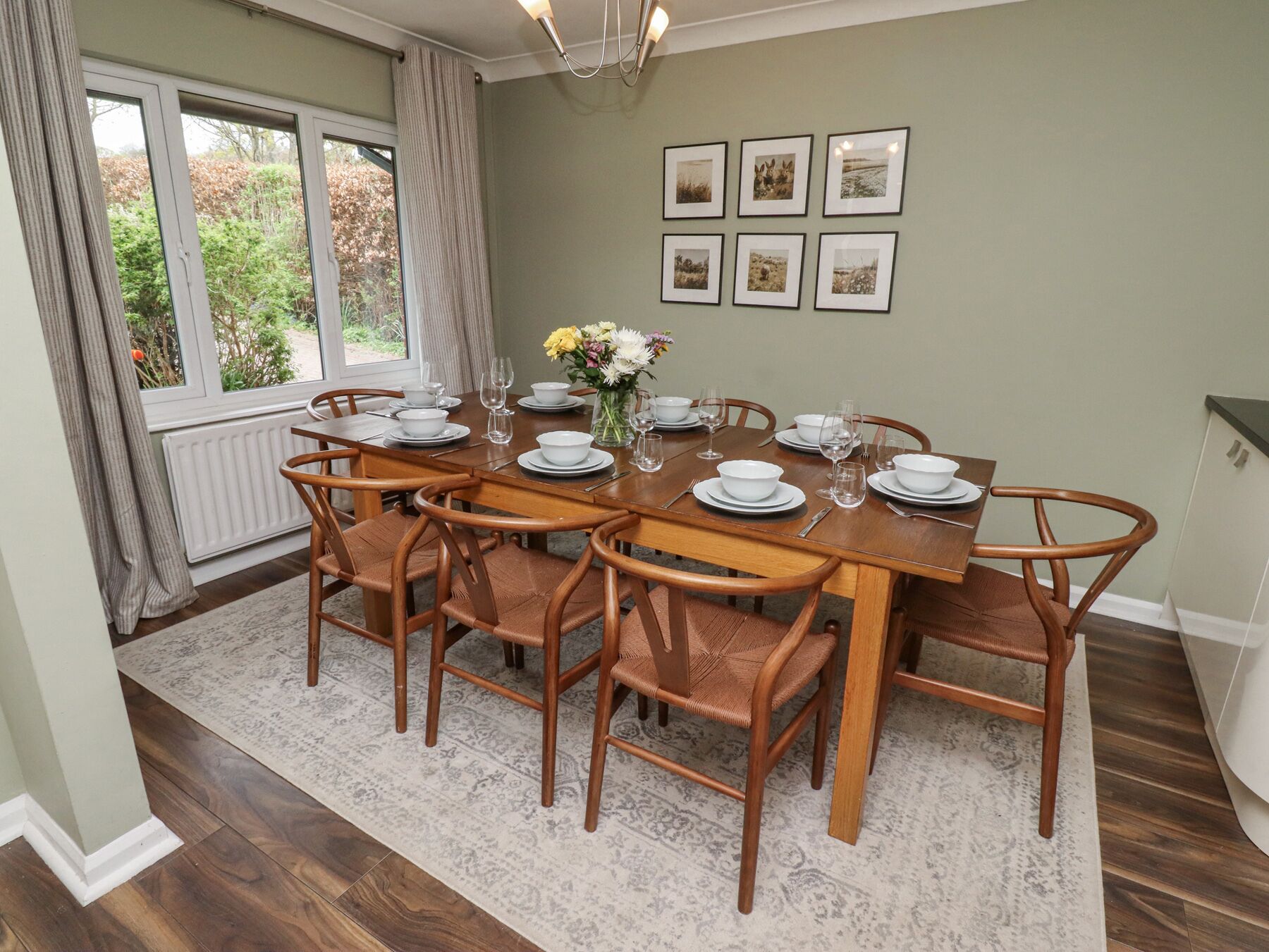 Uma sala de jantar com uma mesa de madeira posta para seis pessoas, rodeada por seis cadeiras de madeira.
