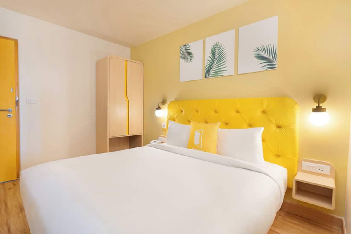 Quarto de hotel com uma cama grande, cabeceira amarela e um guarda-roupa de madeira.