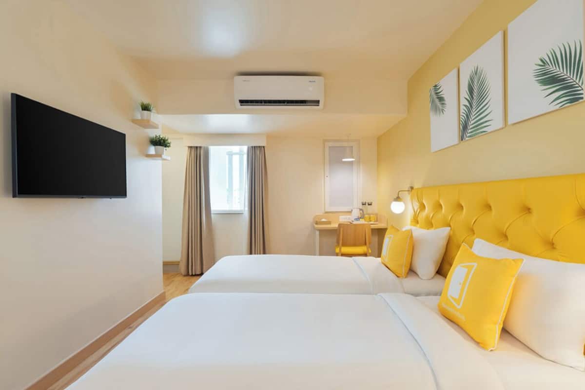 Quarto de hotel com duas camas, televisão de tela plana, ar condicionado, escrivaninha com cadeira e janela com cortinas.
