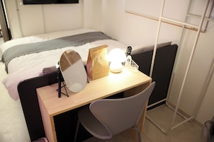 Quarto bem arrumado com cama, escrivaninha, cadeira, abajur e espelho.