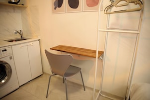 Cozinha compacta com máquina de lavar, bancada de madeira e uma cadeira.