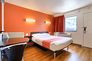 Quarto de hotel com cama, mesa, cadeira, janela com cortinas e ar condicionado.