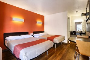 Quarto de hotel com duas camas, uma mesa de jantar e uma cozinha compacta.