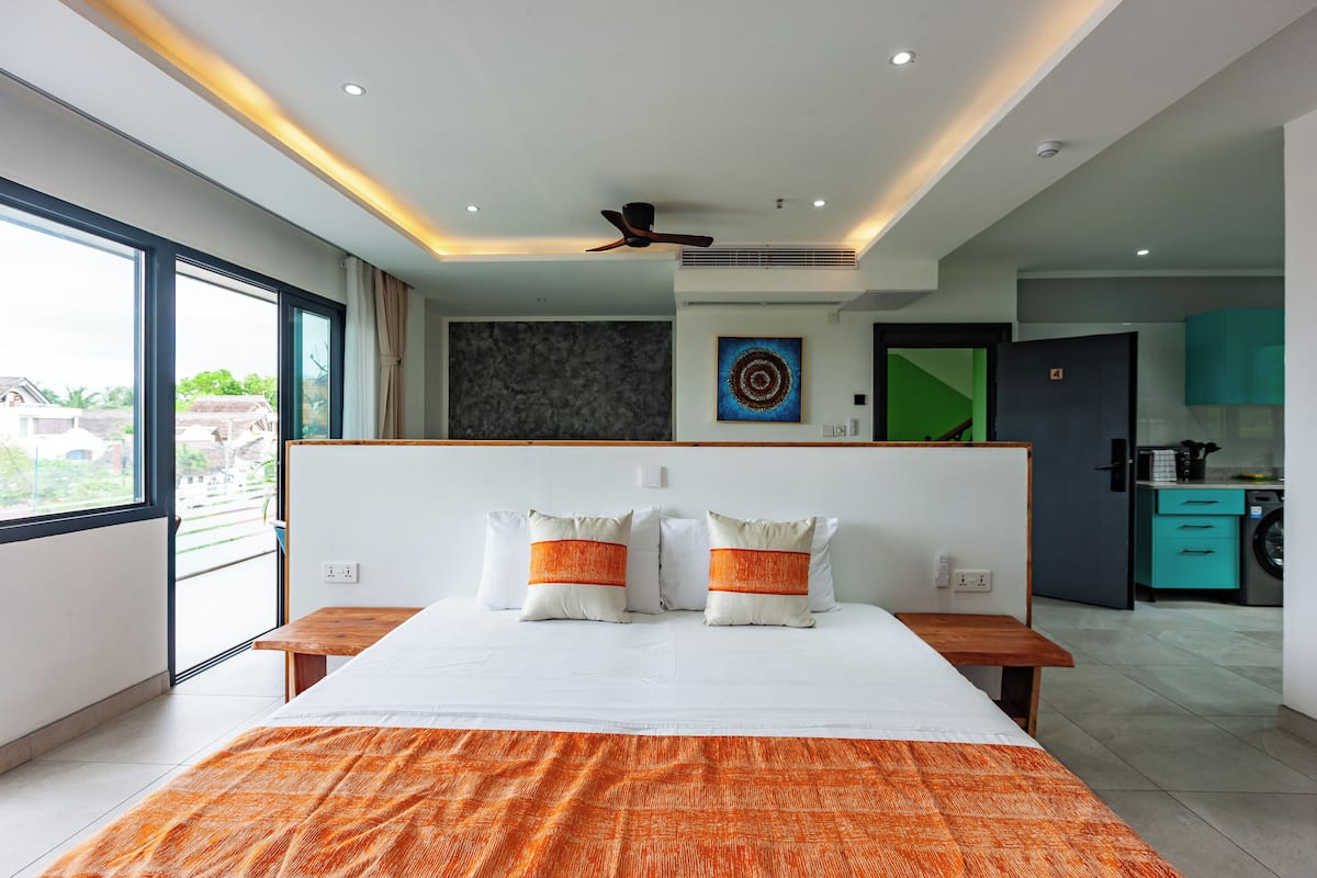 Quarto de hotel moderno com uma cama grande, um ventilador de teto e vista para a cidade.