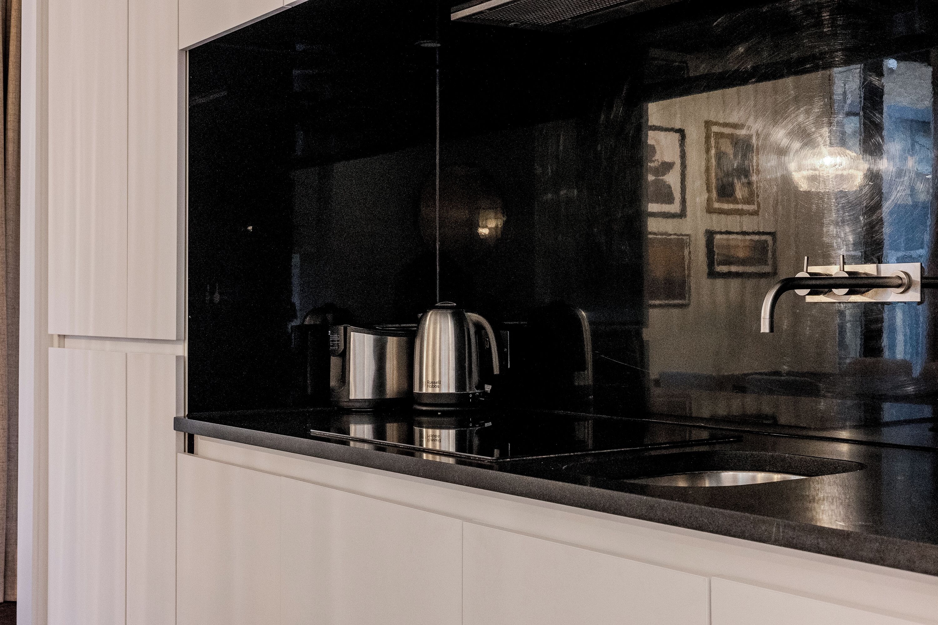 Cozinha com bancada preta, eletrodomésticos de aço inoxidável e armário branco.