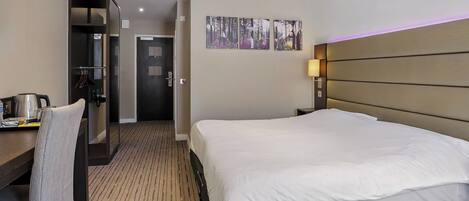 Quarto de hotel com uma cama grande, uma escrivaninha com cadeira, um cabideiro e um quadro na parede.