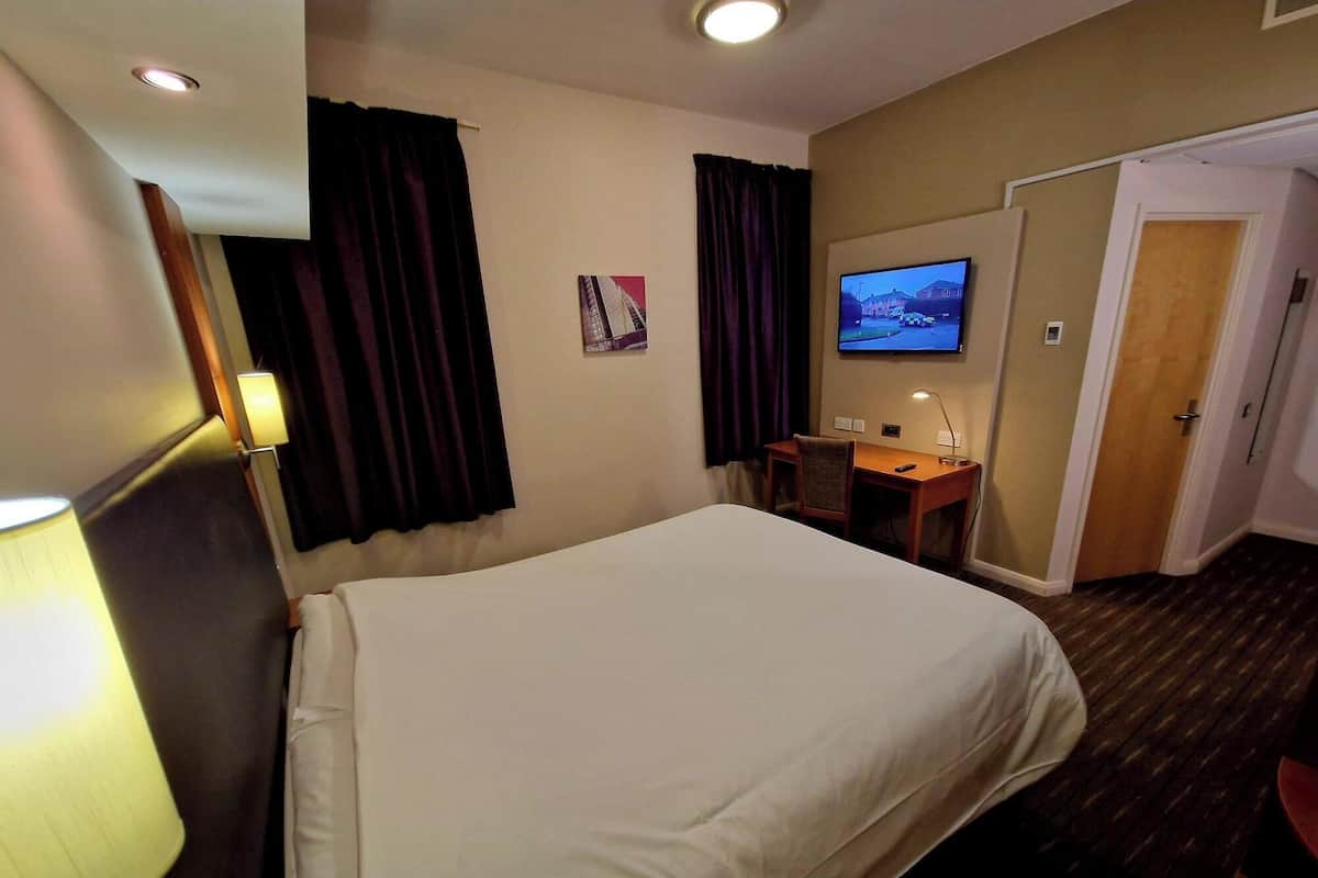 Quarto de hotel com uma cama, uma escrivaninha, uma televisão e uma porta.