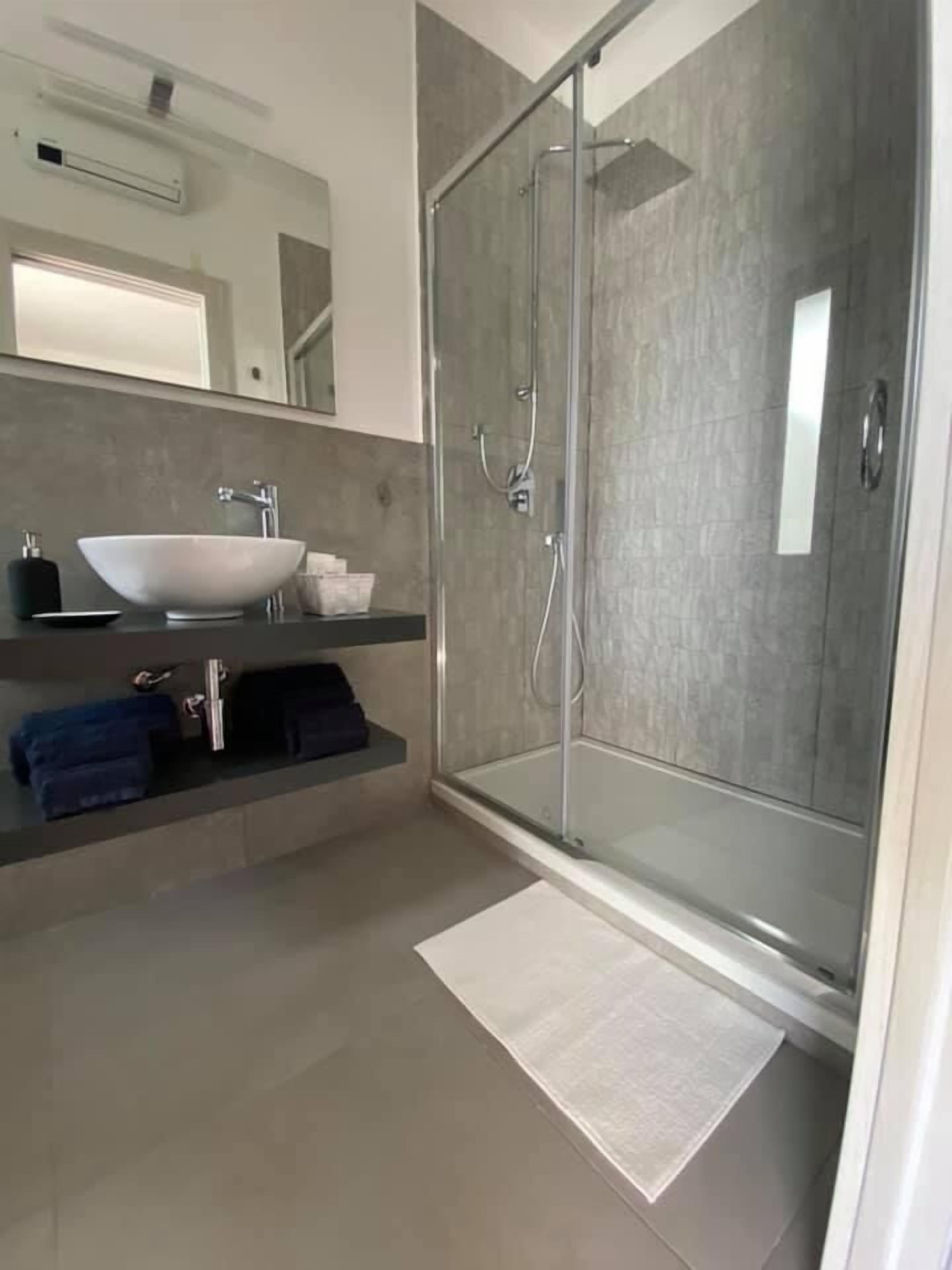 Uma casa de banho moderna com cabine de duche em vidro, lavatório branco e um porta-toalhas.
