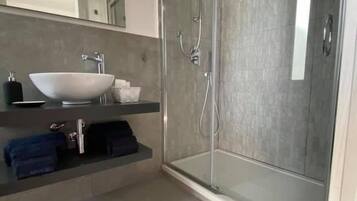 Uma casa de banho moderna com cabine de duche em vidro, lavatório branco e um porta-toalhas.