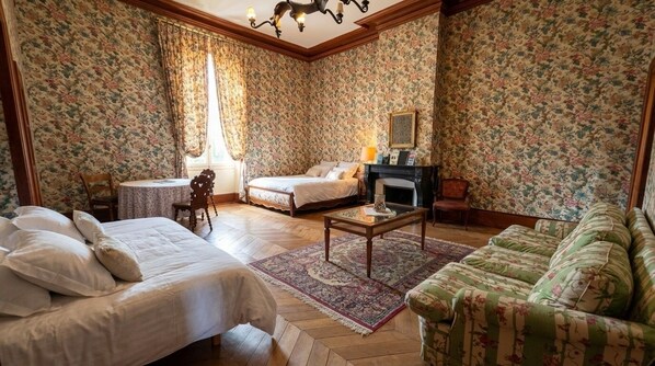 Um quarto com cama, sofá, mesinha, lareira e papel de parede floral.