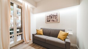 Sala de estar com sofá cinzento, duas almofadas mostarda, um quadro na parede e uma janela com cortinas.