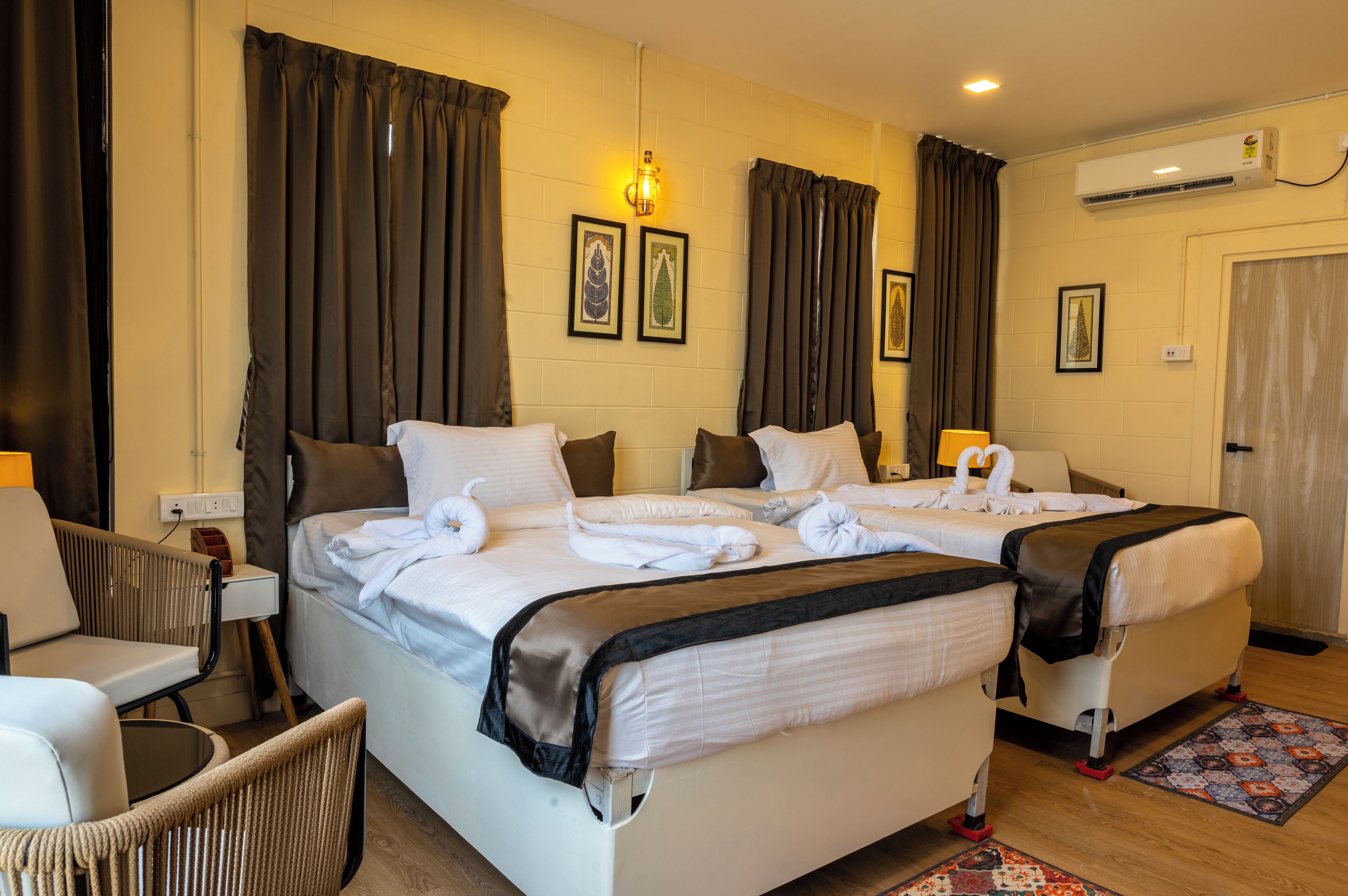 Quarto de hotel com duas camas, uma cadeira, uma mesa e ar condicionado.