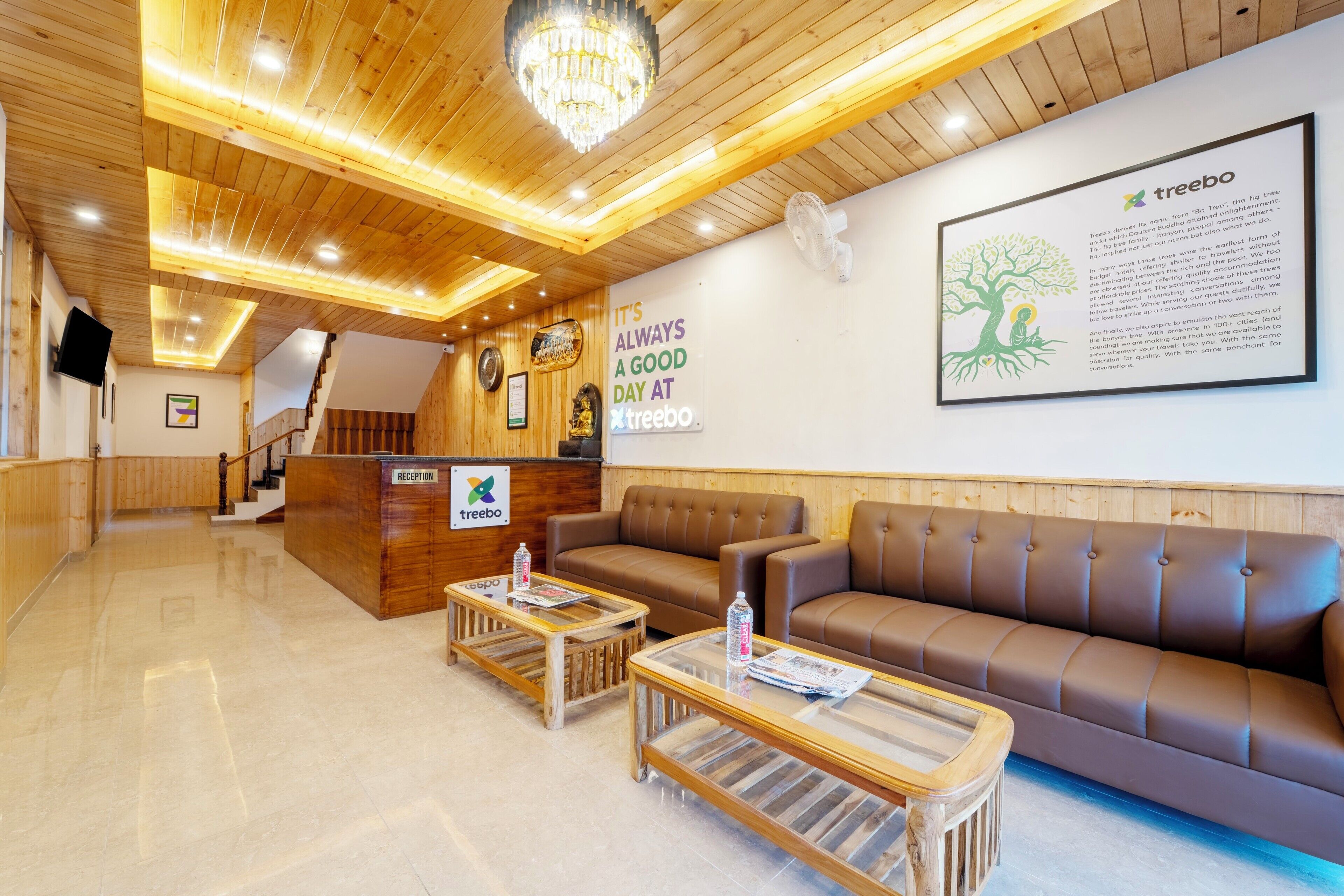 Uma área de recepção com interior em madeira, um candelabro, um balcão de recepção, um sofá de couro marrom e uma placa na parede.