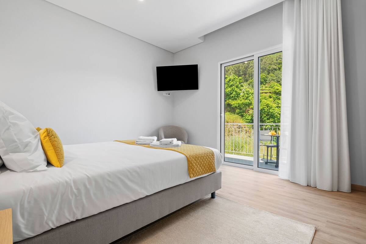 Quarto moderno com uma cama grande, televisão de tela plana na parede e porta de vidro deslizante para uma varanda externa.