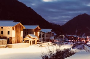 Vila coberta de neve com edifícios de madeira e montanhas ao fundo.