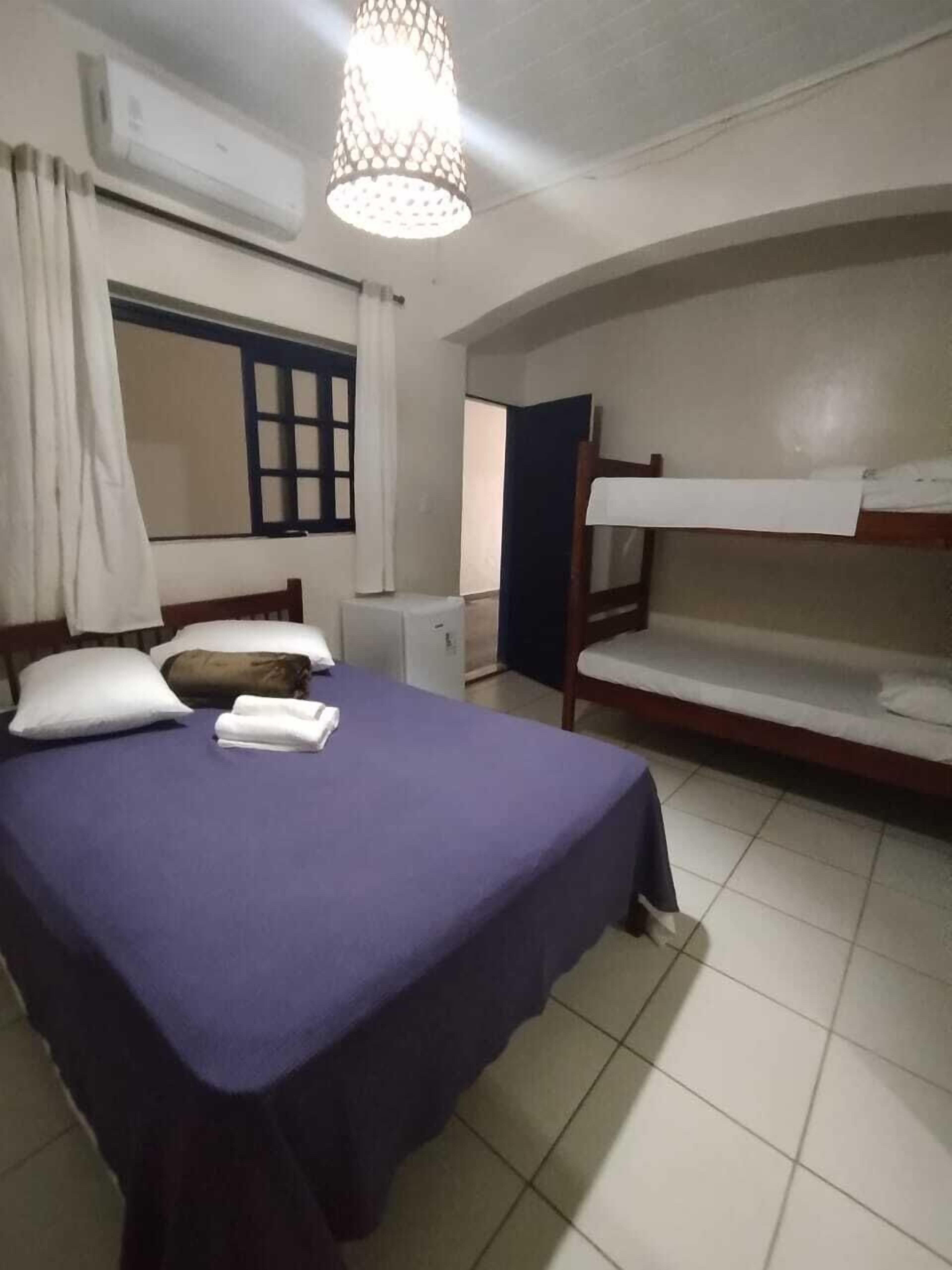 Um quarto com uma cama de solteiro, uma cama beliche, uma janela com cortinas e um ventilador de teto.