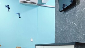 Quarto com parede azul, bancada de mármore preto, televisão fixada na parede e um aviso que diz 'SAÍDA'.