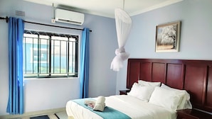 Quarto de hotel com cama, mesa de cabeceira, janela com cortinas, ar condicionado e um quadro na parede.