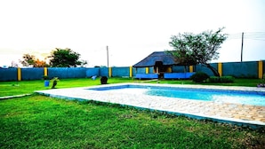 Piscina com deck ladrilhado, cercada por um gramado e um muro baixo azul.