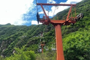 Um sistema de teleférico com cadeiras suspensas de uma estrutura metálica vermelha, com colinas verdejantes ao fundo.