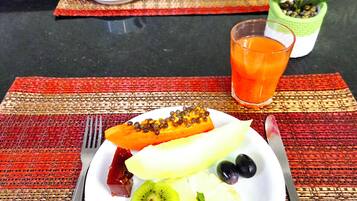 Um cenário de café da manhã com uma travessa de frutas, um copo de suco de laranja e um pequeno vaso de planta.