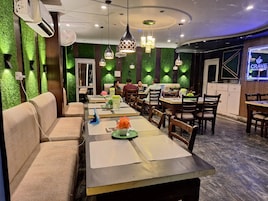 Um restaurante com decoração de parede verde, diversas mesas de jantar e luminárias pendentes.