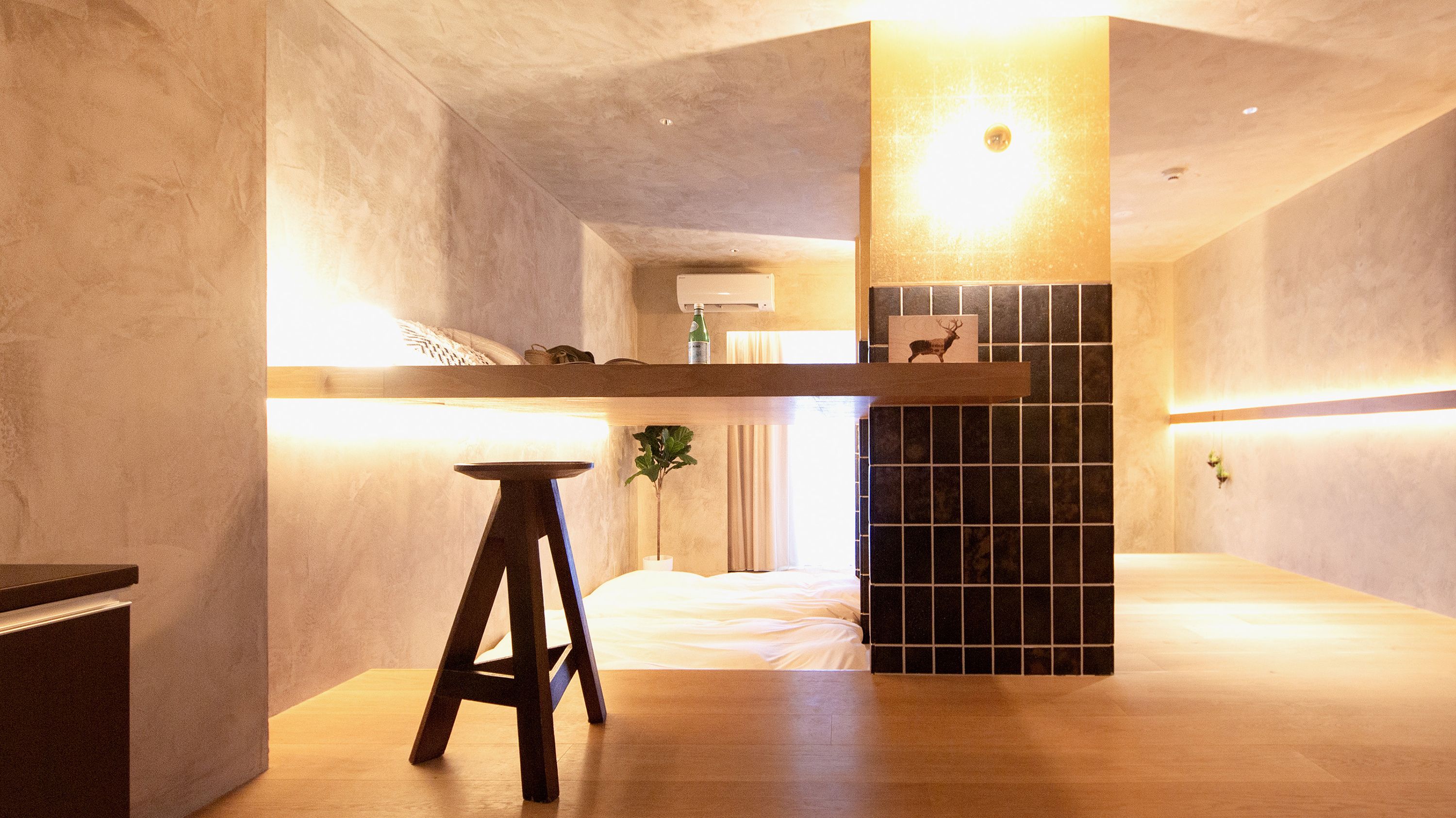Quarto de hotel moderno com beliche, uma mesinha, planta em vaso e prateleira na parede com objeto decorativo.