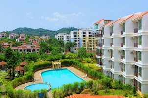 Resort com várias construções, piscina e vegetação exuberante.